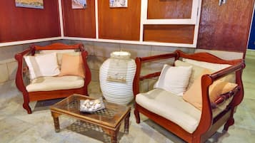 Um quarto com duas poltronas de madeira, uma mesa de centro de vidro e uma pilha de pratos brancos.
