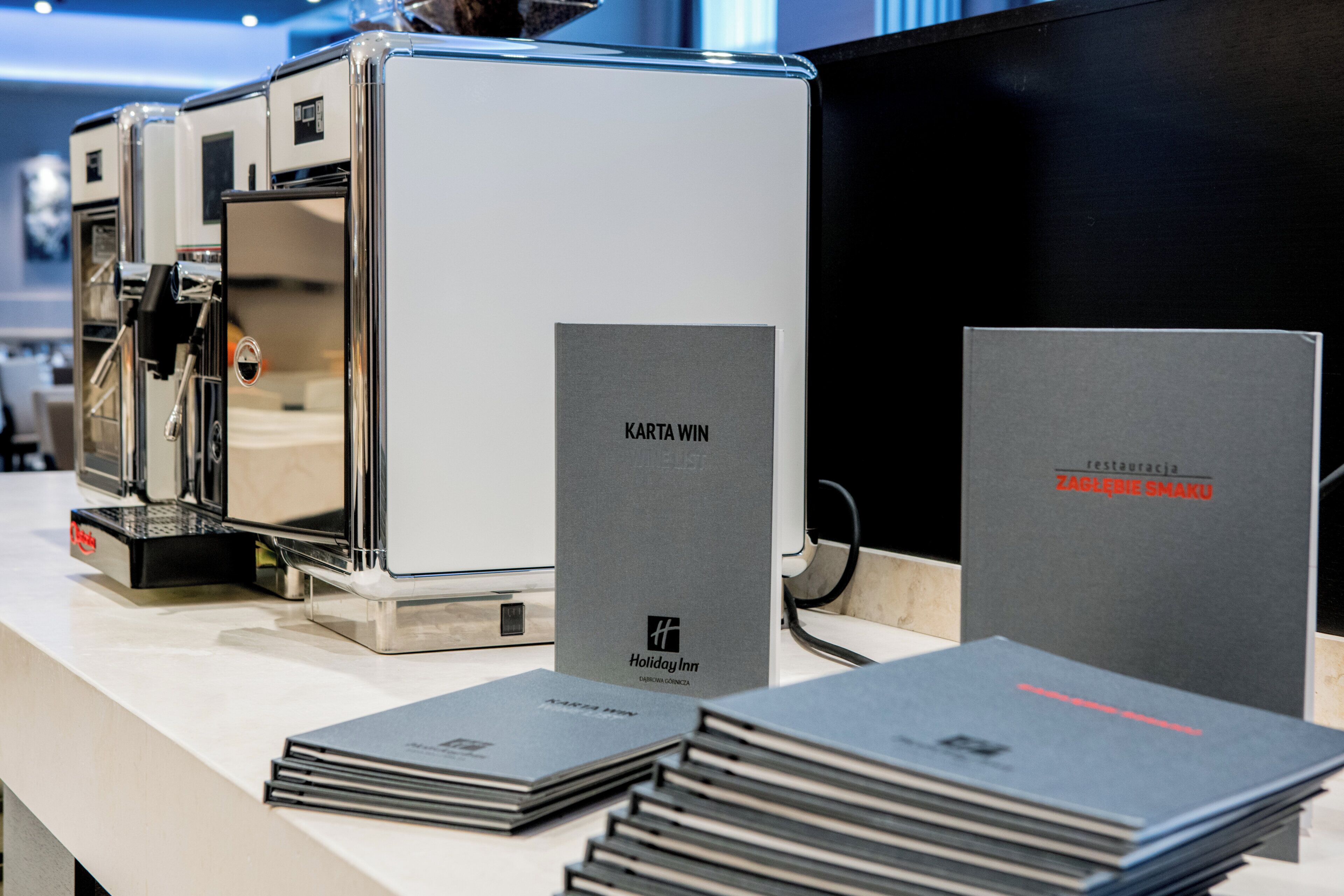 Máquina de café moderna e dois folhetos informativos em um balcão.