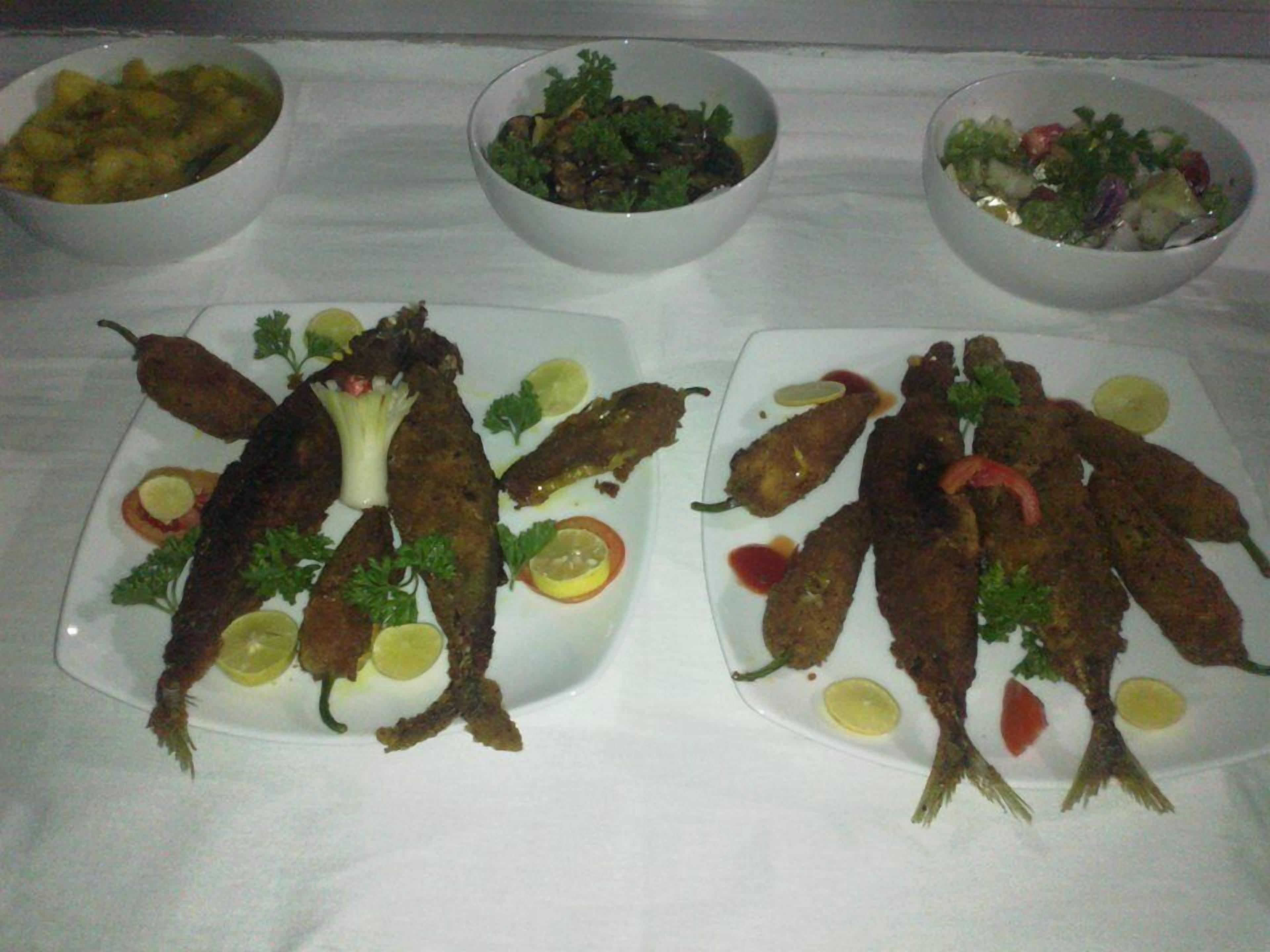 Uma mesa com dois pratos de peixe frito, um tacho de batatas e um tacho de salada.