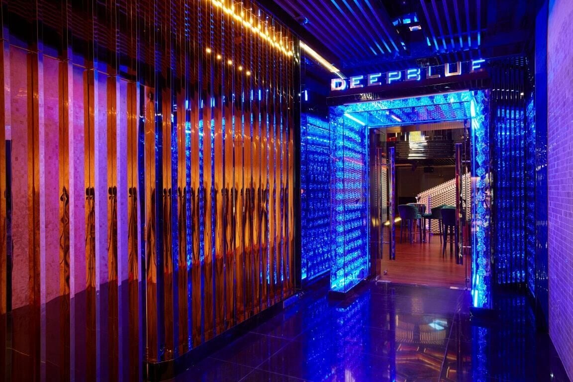 Um interior moderno com uma entrada iluminada em azul e uma placa com a inscrição "DEEPBLUE".