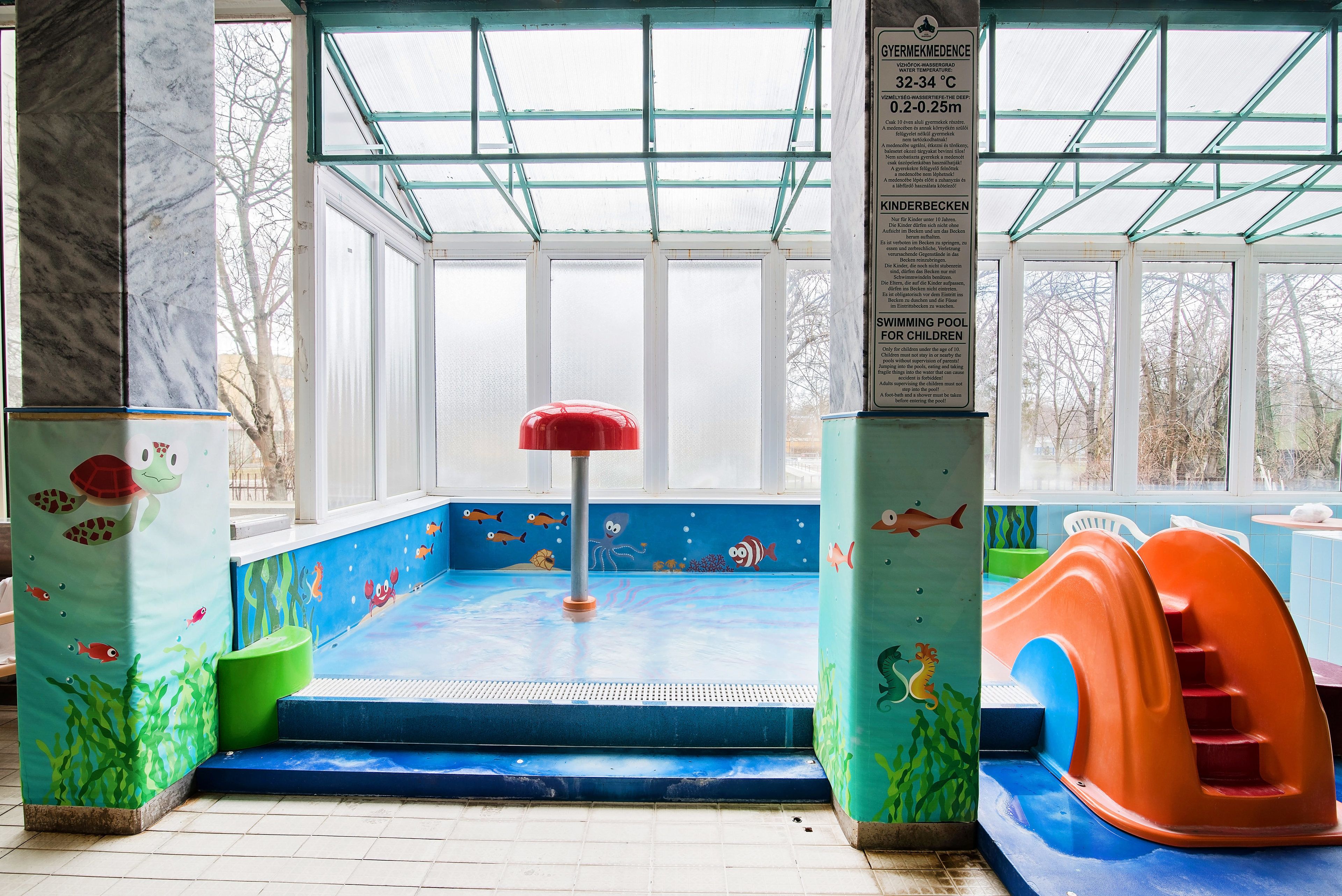Espaço infantil com escorrega, piscina pequena e um mural de paisagem submarina.