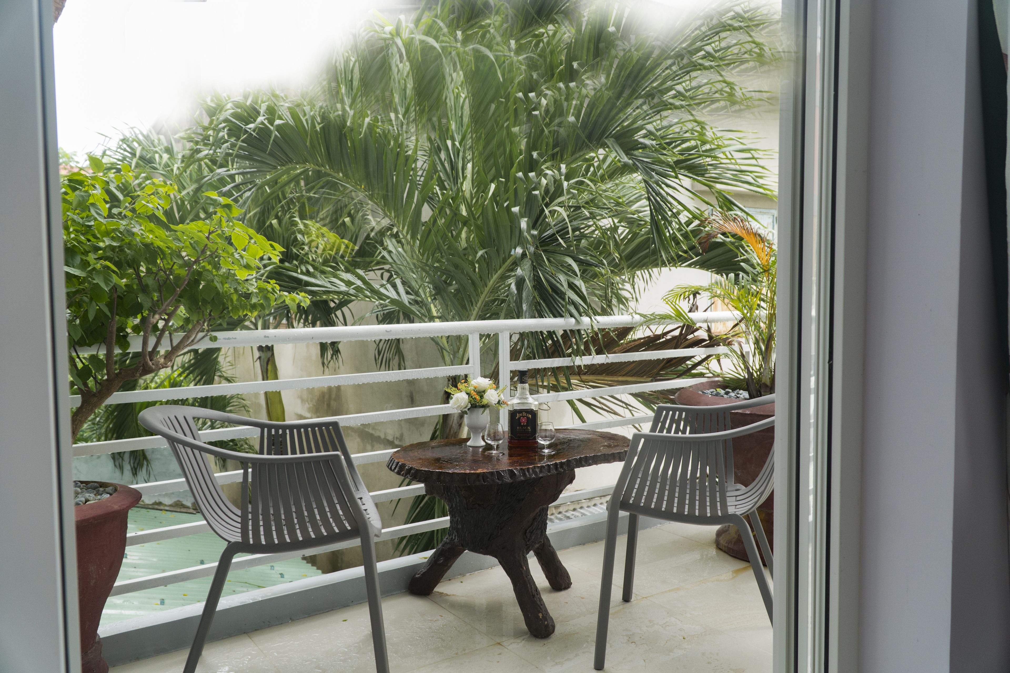 Varanda com mesa redonda e duas cadeiras, um vaso de planta e vista para área verde.