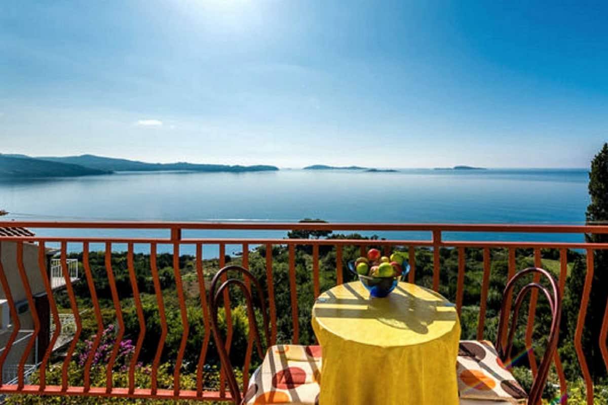 Varanda com mesa e cadeiras, vista para um lago tranquilo e ilhas ao longe.