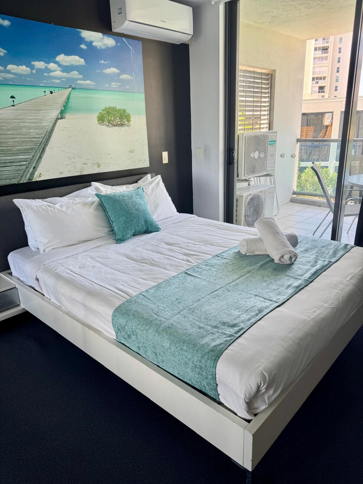 Quarto de hotel moderno com uma cama grande, vista para um cais e varanda com vista para a cidade.