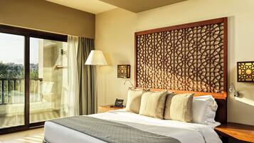 Quarto de hotel com uma cama grande, varanda, painel decorativo na parede, mesa de cabeceira com luminária e telefone.
