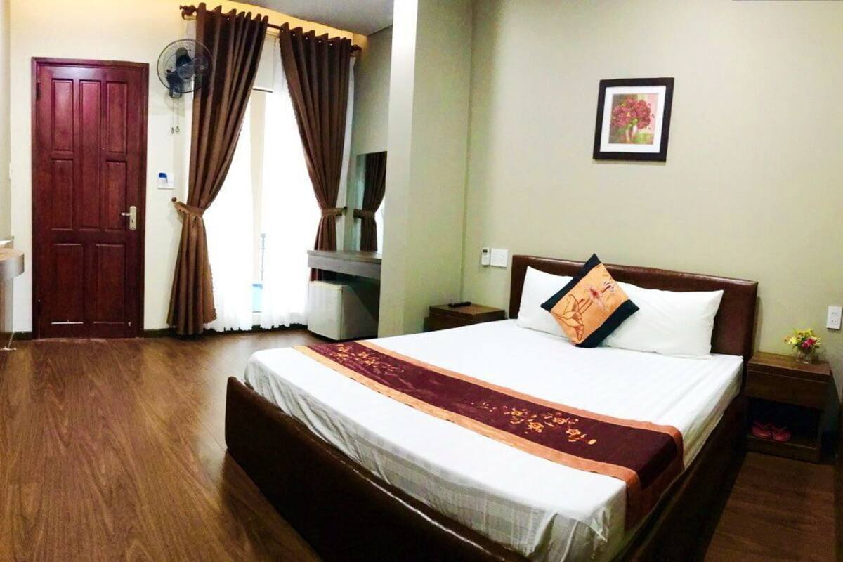 Quarto de hotel com cama, escrivaninha, cadeira, porta e janela com cortinas.