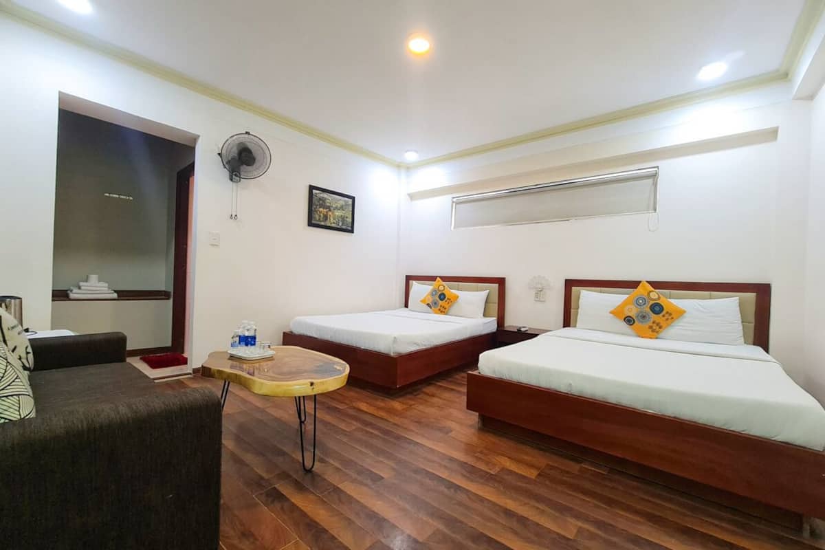 Quarto de hotel com duas camas, um sofá, uma mesa redonda pequena e um ventilador de teto.