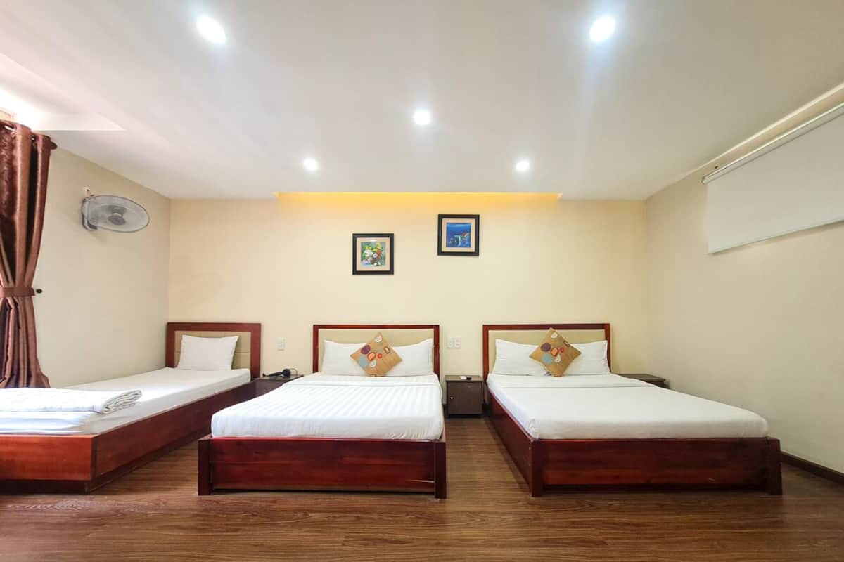 Quarto de hotel com três camas de madeira, um ventilador de teto e duas molduras na parede.