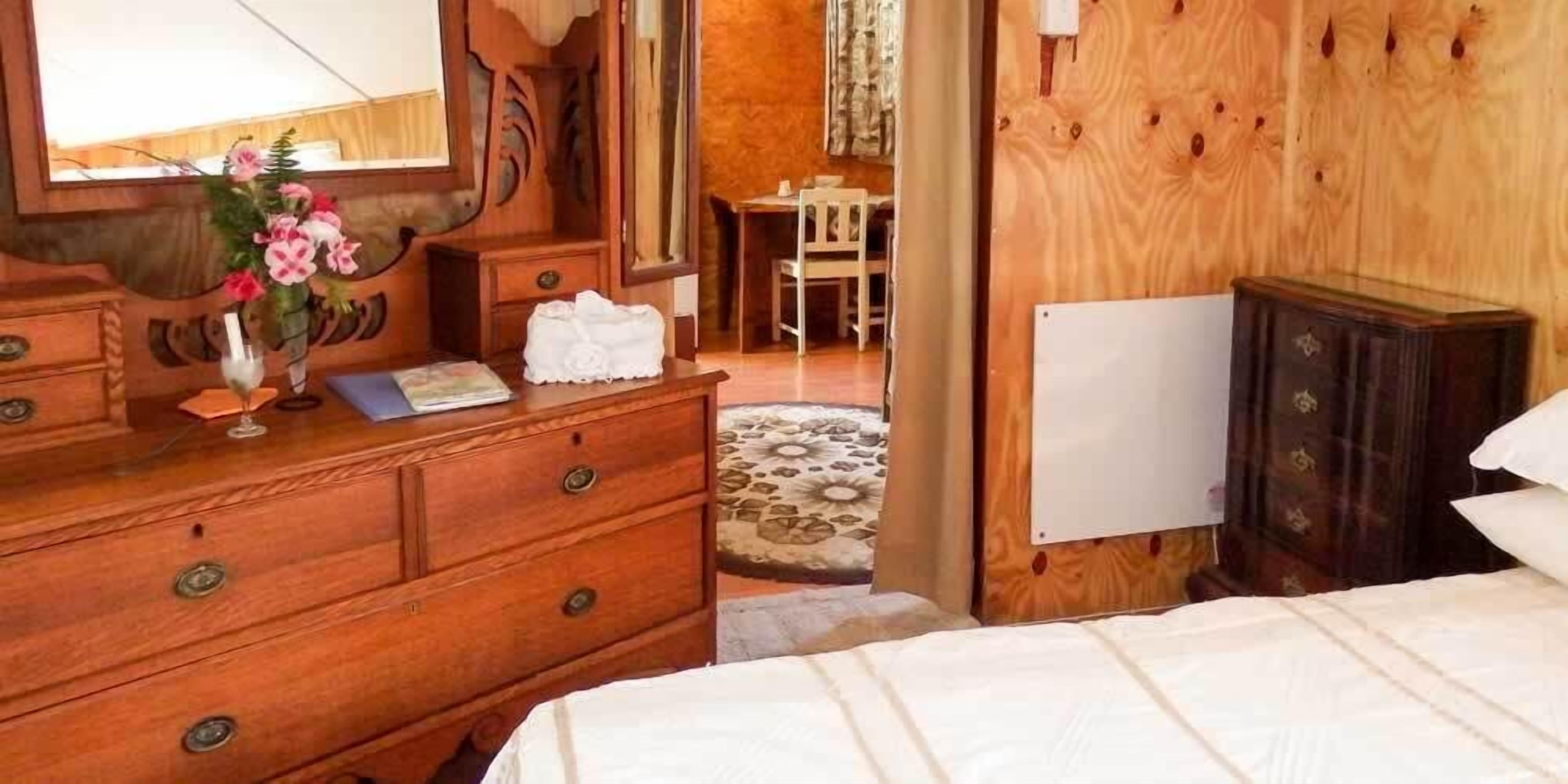 Quarto de madeira com cama, penteadeira, espelho e uma pequena mesa com uma cadeira.