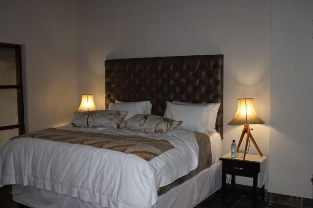 Cama bem arrumada com edredom branco e almofadas estampadas, com duas mesas de cabeceira e abajures de cada lado.