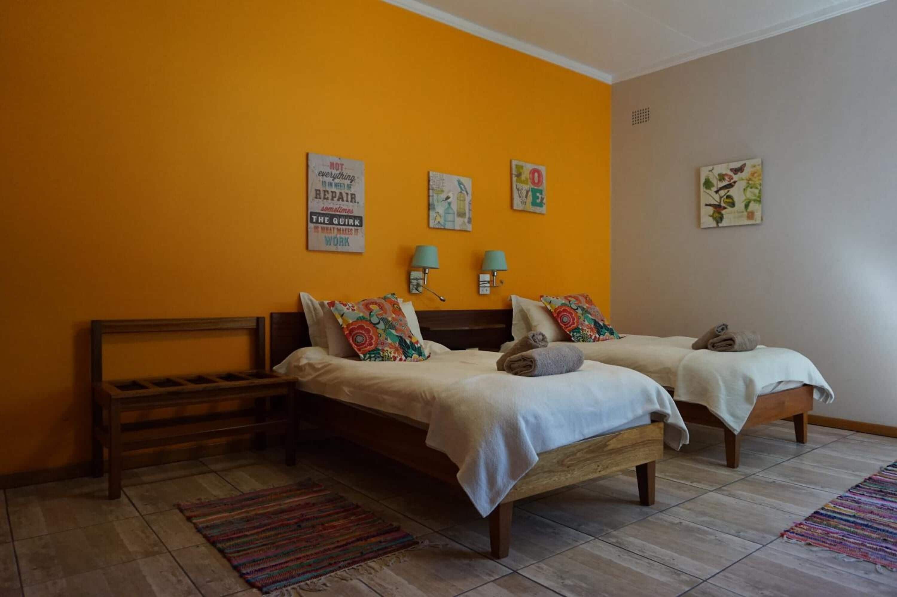 Quarto com duas camas, um banco e um tapete colorido.