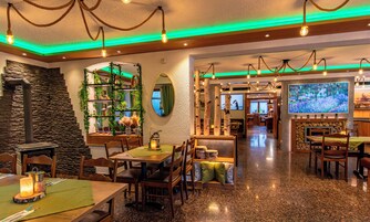 Interior de restaurante com parede de pedra, mesas e cadeiras de madeira. Há luminárias pendentes e um quadro grande na parede.
