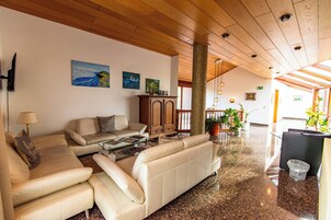 Um hall amplo com teto alto, uma coluna de madeira e um espaço de estar com sofá e poltronas.