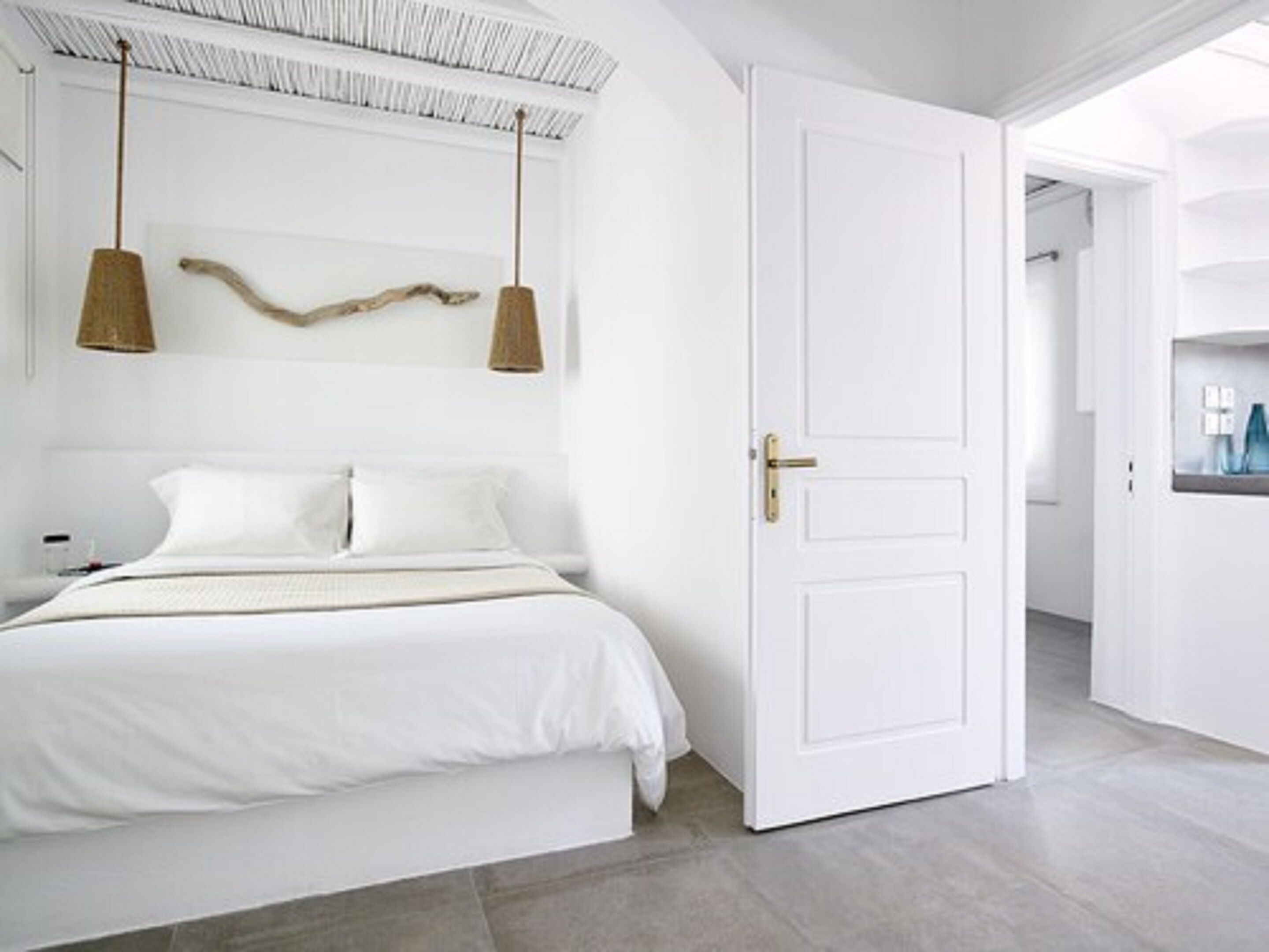 Quarto de hotel moderno com uma cama grande, uma porta branca e vista para outro quarto.