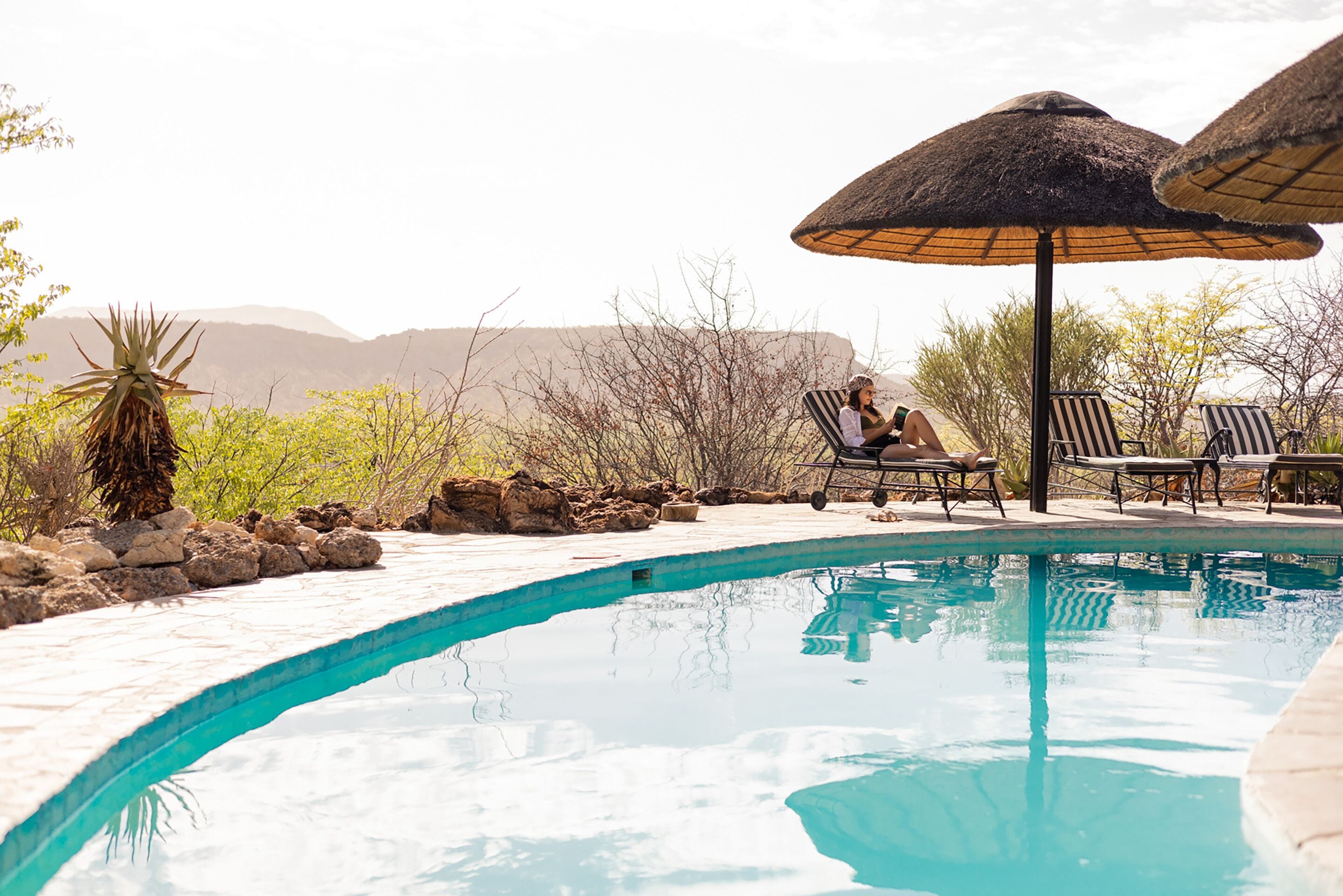 Uma área de piscina com espreguiçadeiras e guarda-sóis, rodeada por vegetação de deserto e pedras.