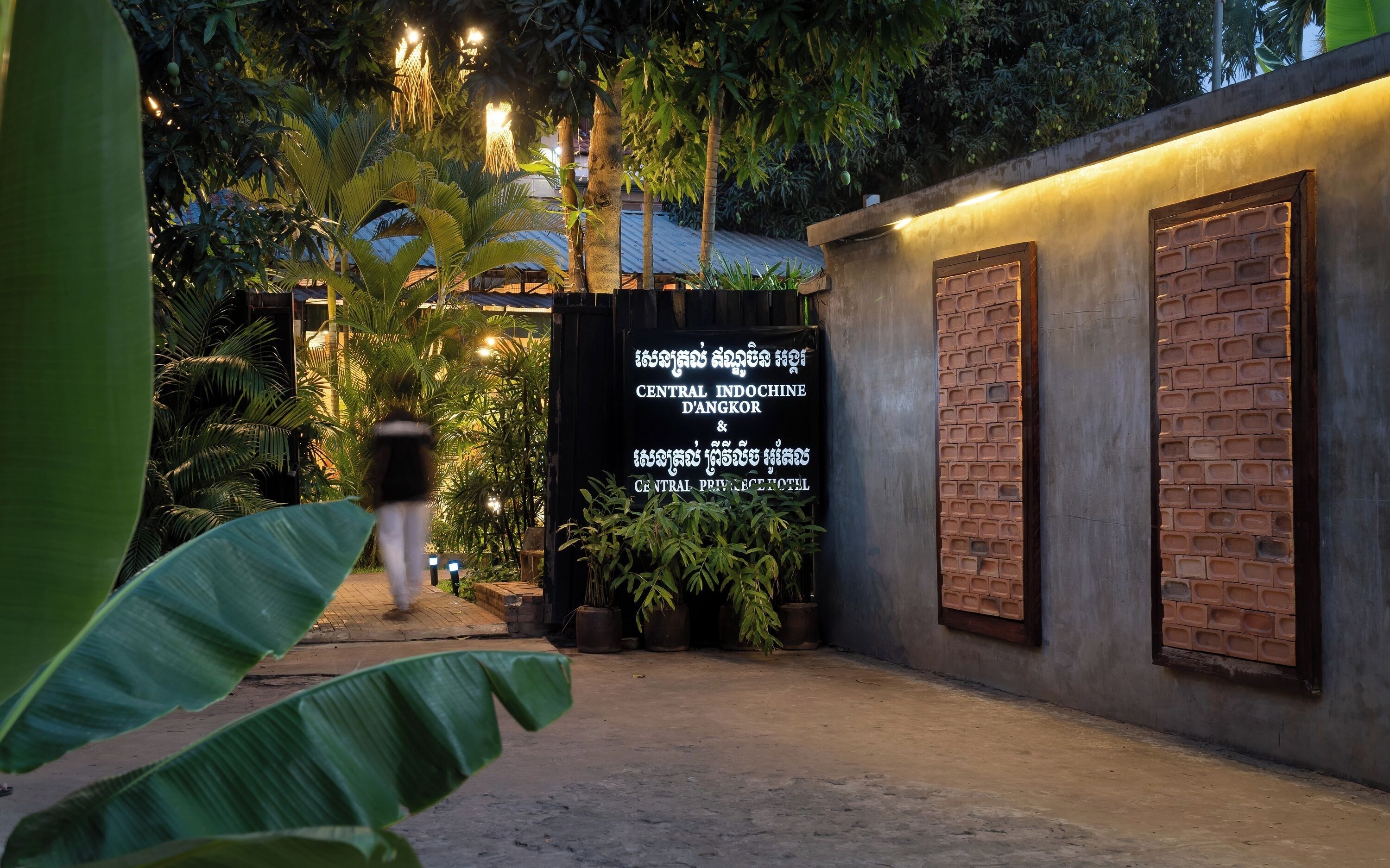 Placa para Central Indochine D'Angkor & Central Private Hotel, cercada por vegetação exuberante e uma parede de tijolos.