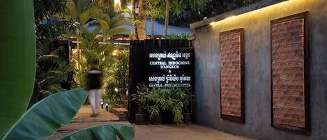 Placa para Central Indochine D'Angkor & Central Private Hotel, cercada por vegetação exuberante e uma parede de tijolos.