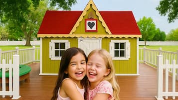 Duas crianças se abraçando em frente a uma casinha colorida com telhado vermelho e um símbolo de coração na porta.