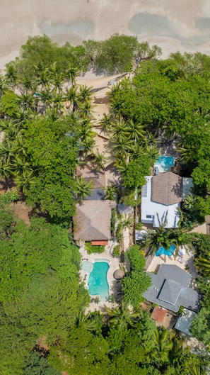 Vista aérea de um resort com piscina, palmeiras e área de praia.