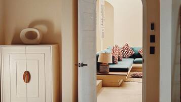 Quarto com cama, guarda-roupa e porta que dá para outro ambiente com sofá e abajur.
