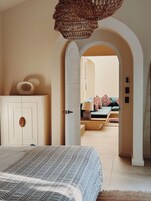 Quarto com cama, guarda-roupa e porta que dá para outro ambiente com sofá e abajur.