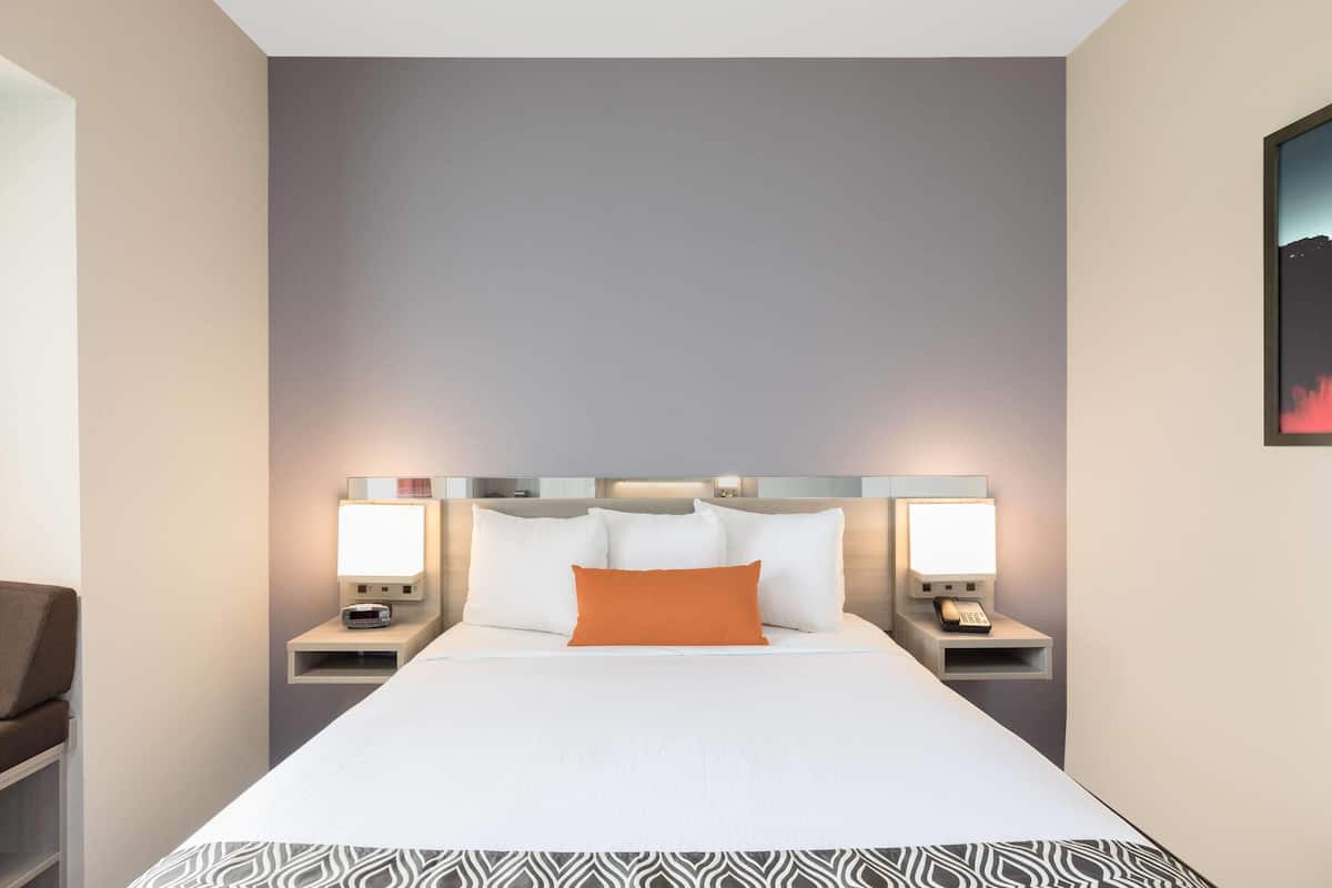 Quarto de hotel com uma cama grande, duas mesas de cabeceira com abajures e uma mesinha de apoio com telefone.