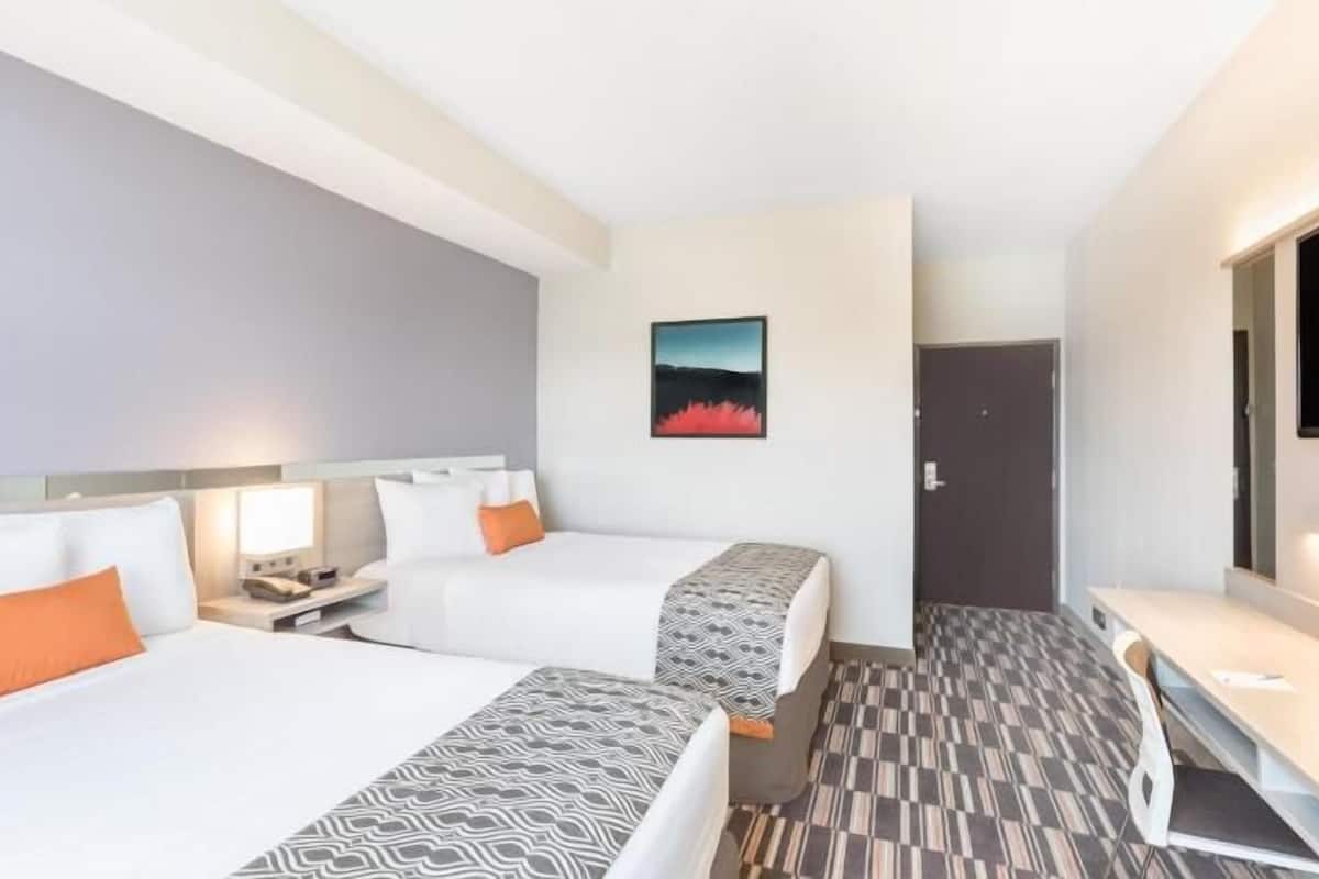 Quarto de hotel com duas camas, uma escrivaninha, televisão e um quadro na parede.