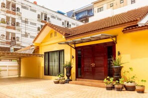 Um edifício amarelo com telhado telhado, porta de madeira e vasos de plantas.