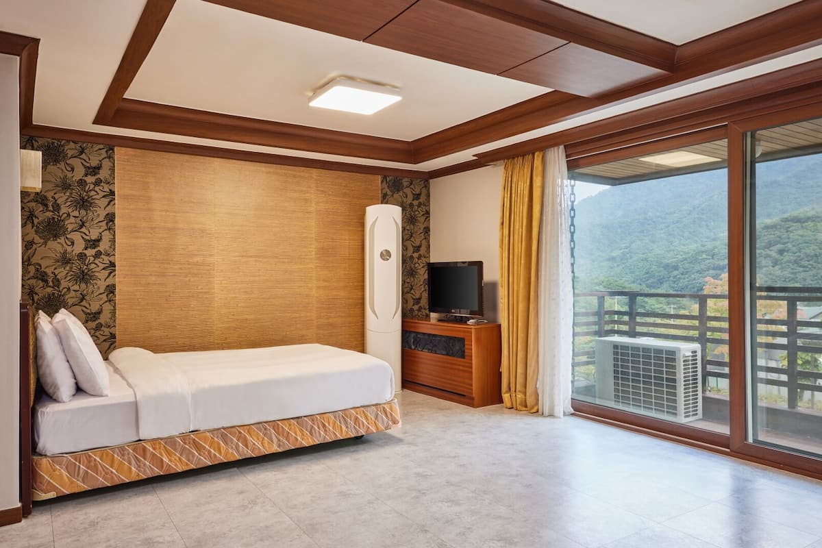 Quarto de hotel com cama, televisão, frigobar e varanda com vista para as montanhas.