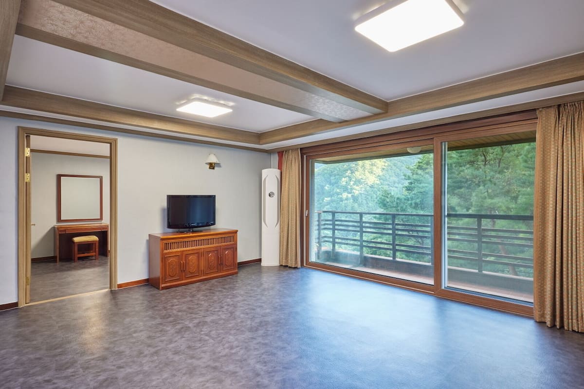 Quarto espaçoso com uma grande porta de vidro deslizante que dá para uma varanda, um armário de madeira com uma televisão e um espelho na parede.