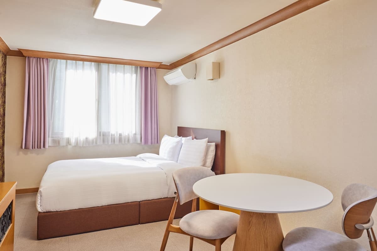 Quarto de hotel com uma cama, uma mesinha redonda e uma cadeira.