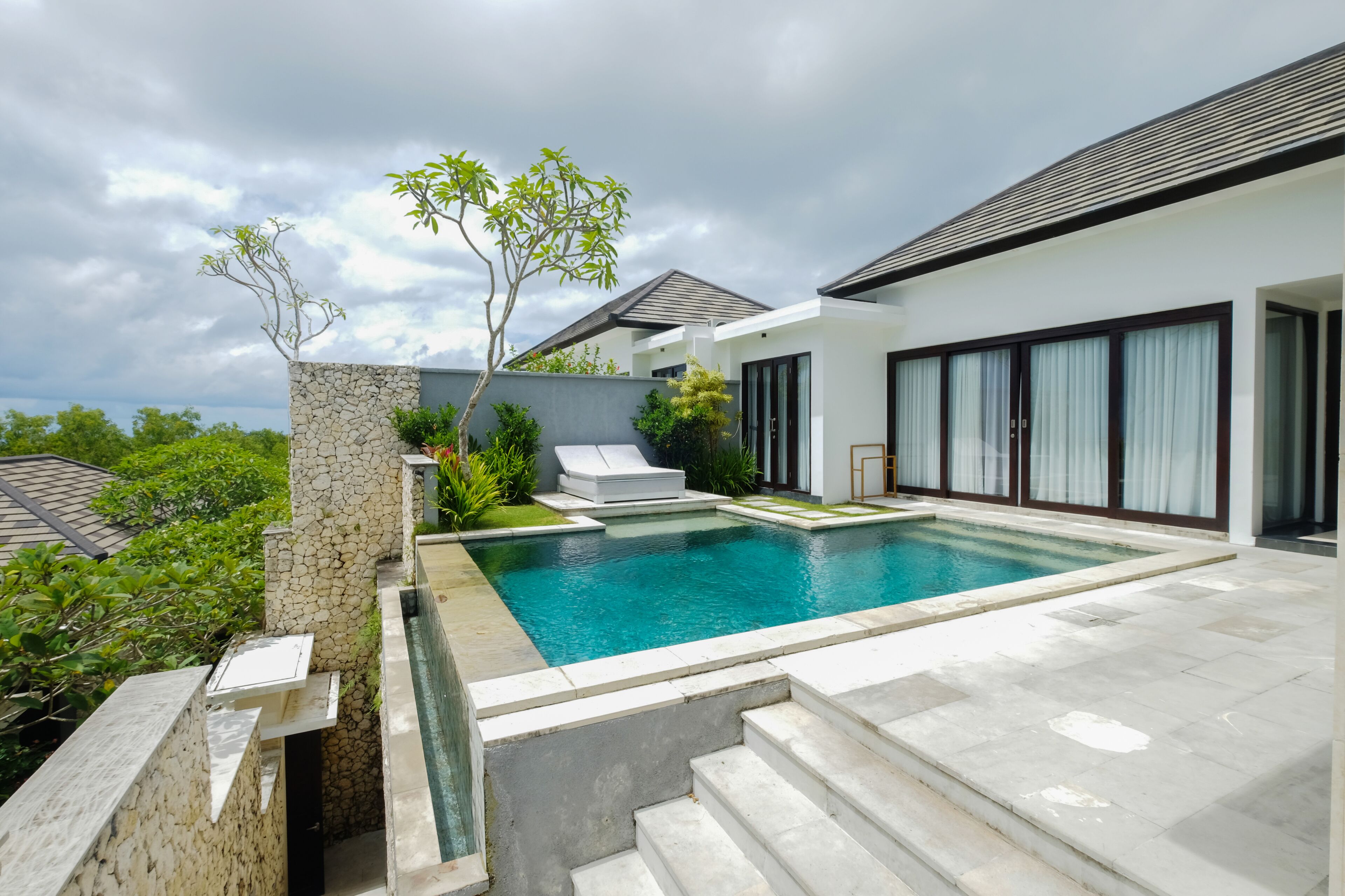 Uma casa moderna com piscina, paredes de pedra e vista para o oceano.