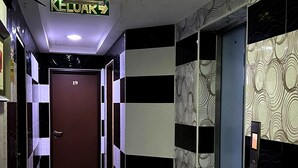 Um corredor com piso listrado em preto e branco, uma porta com a inscrição '19' e uma parede com desenho circular.