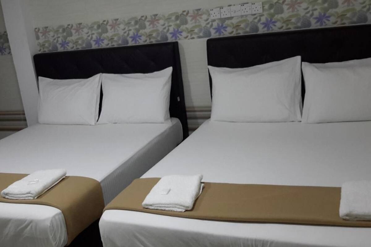 Duas camas de solteiro com roupa de cama branca, cabeceiras marrons e uma parede ao fundo com padrão floral.