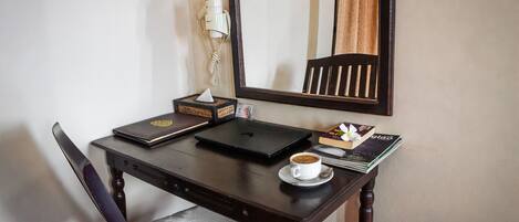 Uma mesa de madeira com um laptop, uma chávena de café, um livro e um secador de cabelo preso na parede.