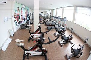 Uma academia com várias máquinas de exercício, janelas amplas e um espelho grande na parede.