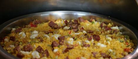 Uma travessa de metal redonda com arroz amarelo, ovos, salsicha e legumes.
