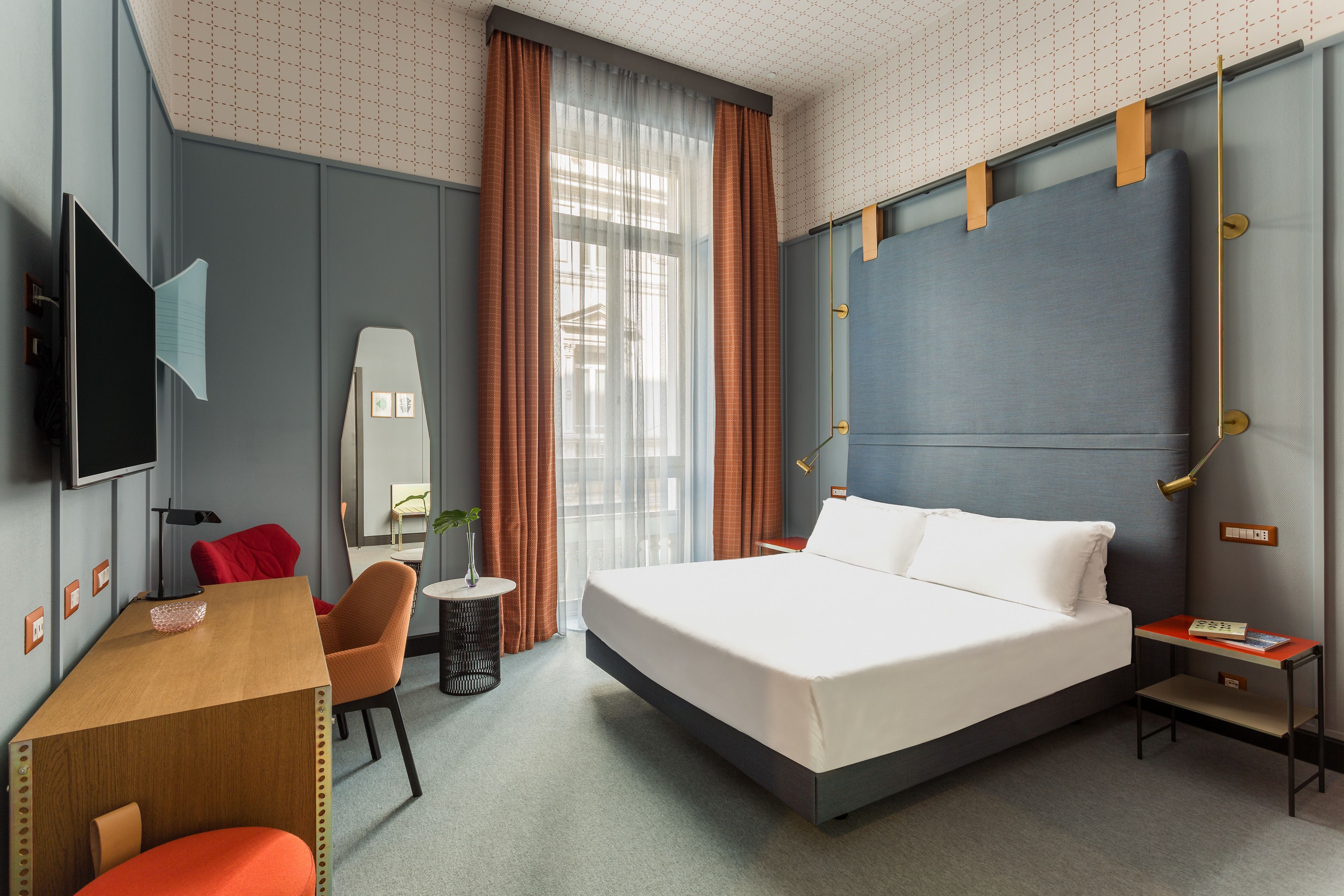Quarto de hotel moderno com uma cama grande, uma escrivaninha, uma televisão e um espaço para sentar.