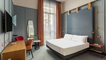 Quarto de hotel moderno com uma cama grande, uma escrivaninha, uma televisão e um espaço para sentar.