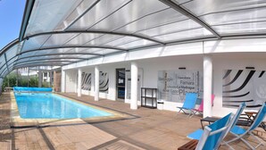 Área de piscina coberta com teto de vidro, cadeiras de descanso e uma parede com diversos nomes de lugares.