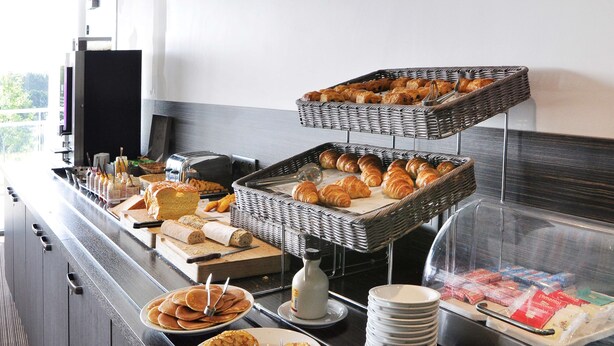 Buffet com diversos itens de café da manhã, incluindo pães, bolos e acompanhamentos.