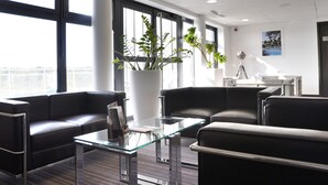 Um espaço de escritório moderno com sofás de couro preto, uma mesa de centro de vidro e plantas em vasos.