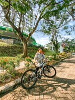 Uma pessoa ao lado de uma bicicleta em um caminho pavimentado, com um edifício identificado como “ibis styles” ao fundo.