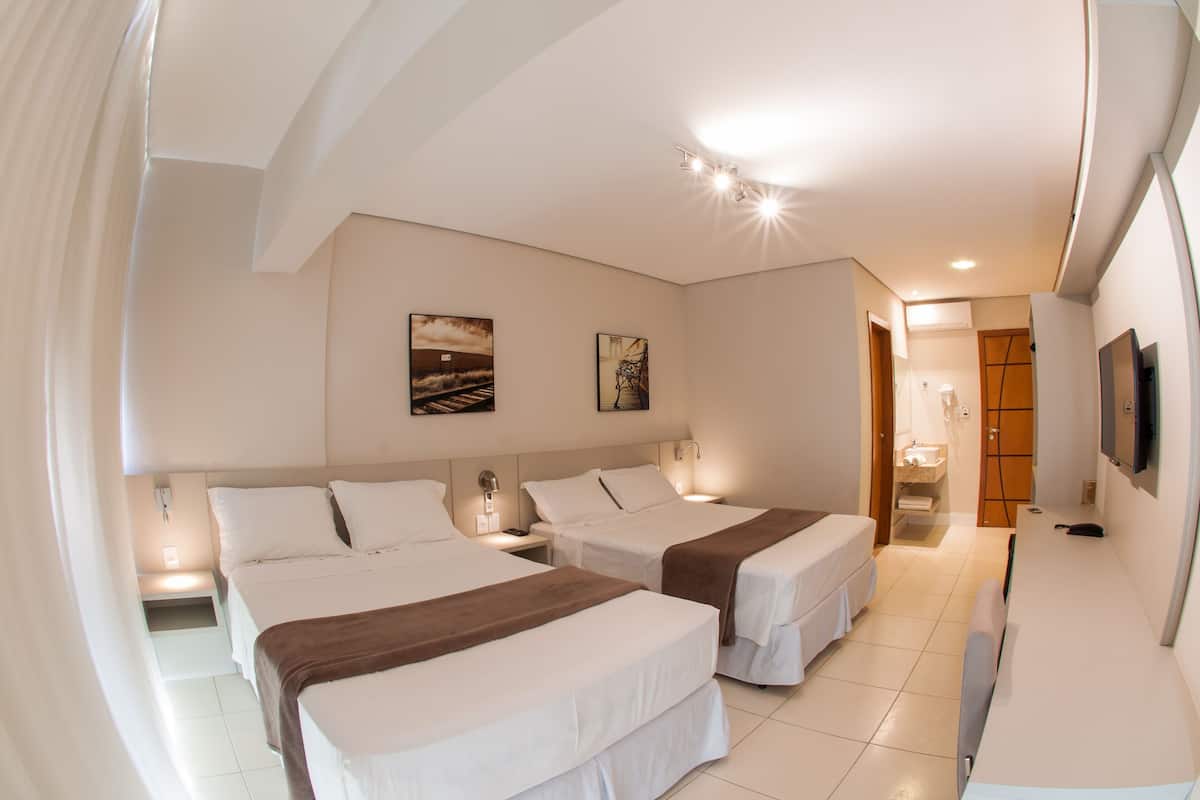 Quarto de hotel com duas camas, televisão e banheiro com pia e espelho.