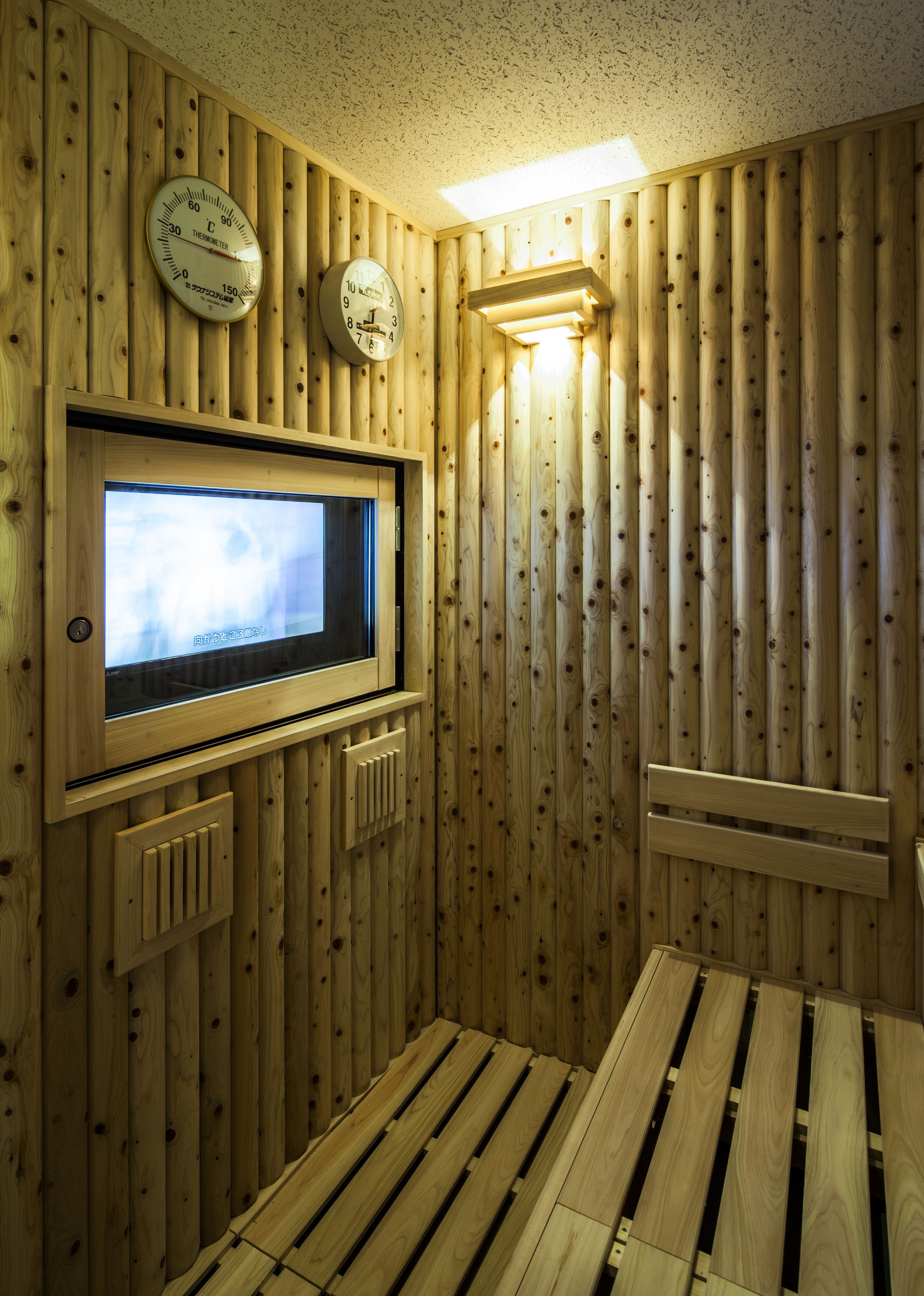 Uma sala de sauna com paredes de madeira, uma tela de televisão e dois termômetros.