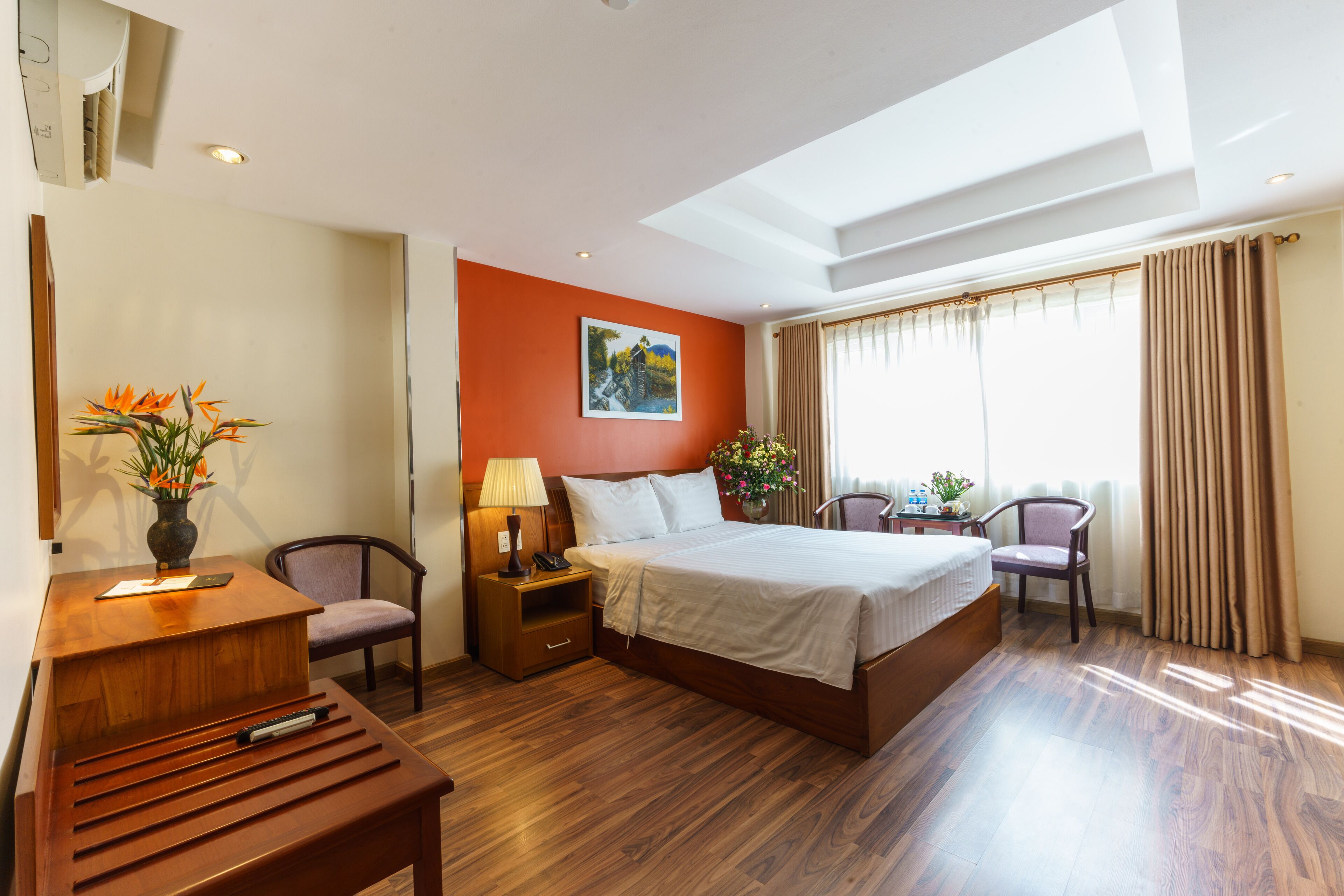 Quarto de hotel com uma cama, escrivaninha, cadeira, mesa de cabeceira, abajur e um quadro na parede.