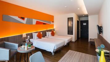 Quarto de hotel moderno com duas camas, um espaço de estar e uma parede de destaque laranja vibrante.