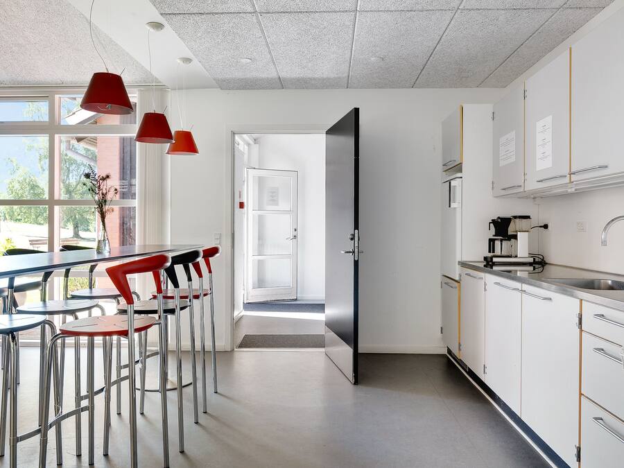 Cozinha moderna com armários brancos, eletrodomésticos de aço inoxidável e luminárias pendentes vermelhas.