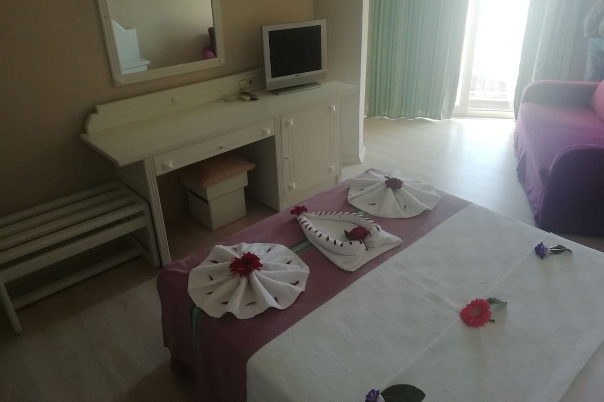 Quarto de hotel com cama, televisão, escrivaninha e cadeira.