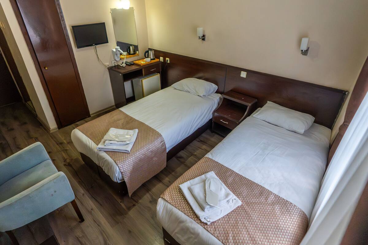 Quarto de hotel com duas camas, uma escrivaninha com telefone e uma cadeira.
